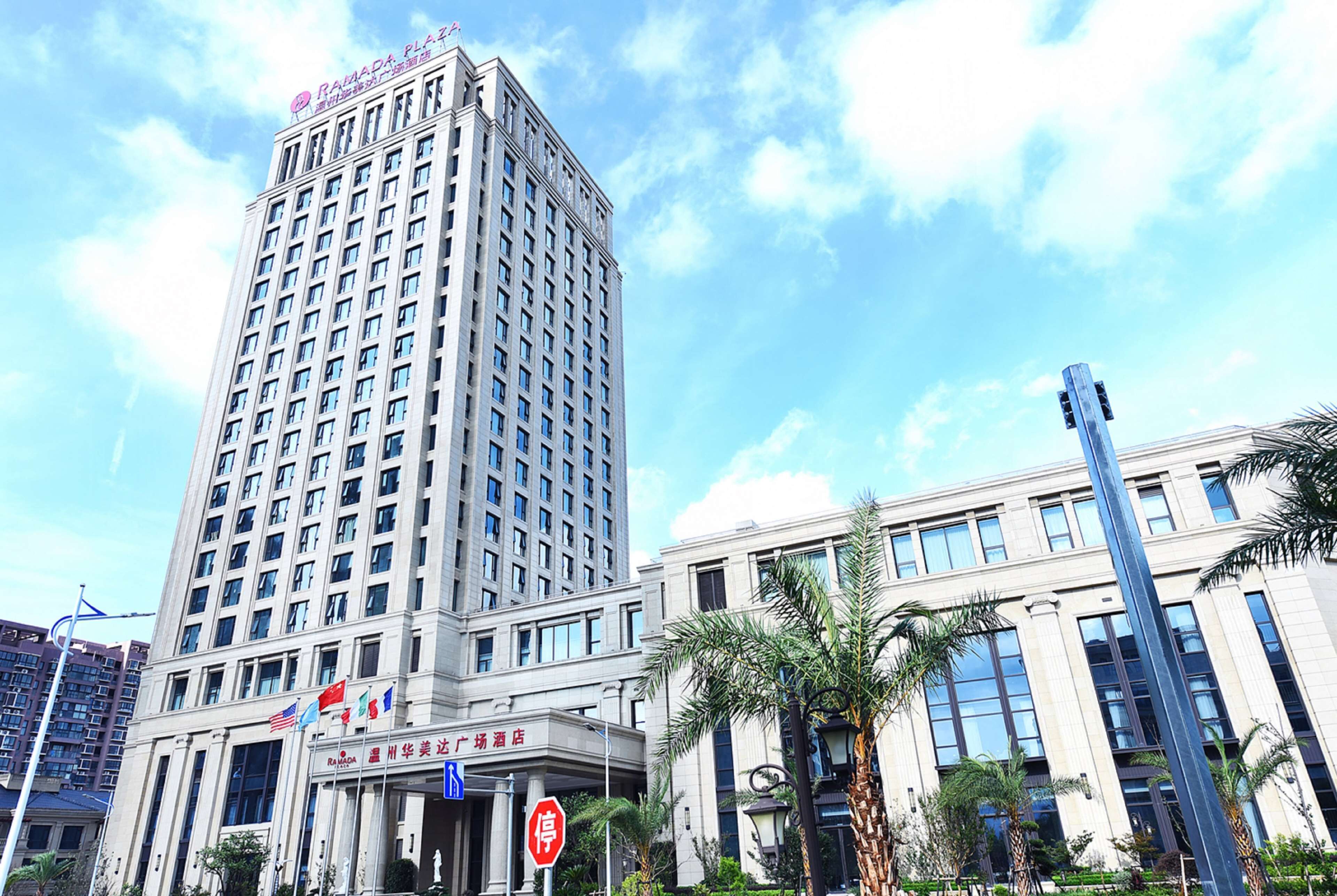 Um edifício alto de hotel com vários andares, entrada destacada com bandeiras e céu claro.
