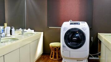 Casa de banho de hotel compacta com máquina de lavar roupa, lavatório e um banquinho.