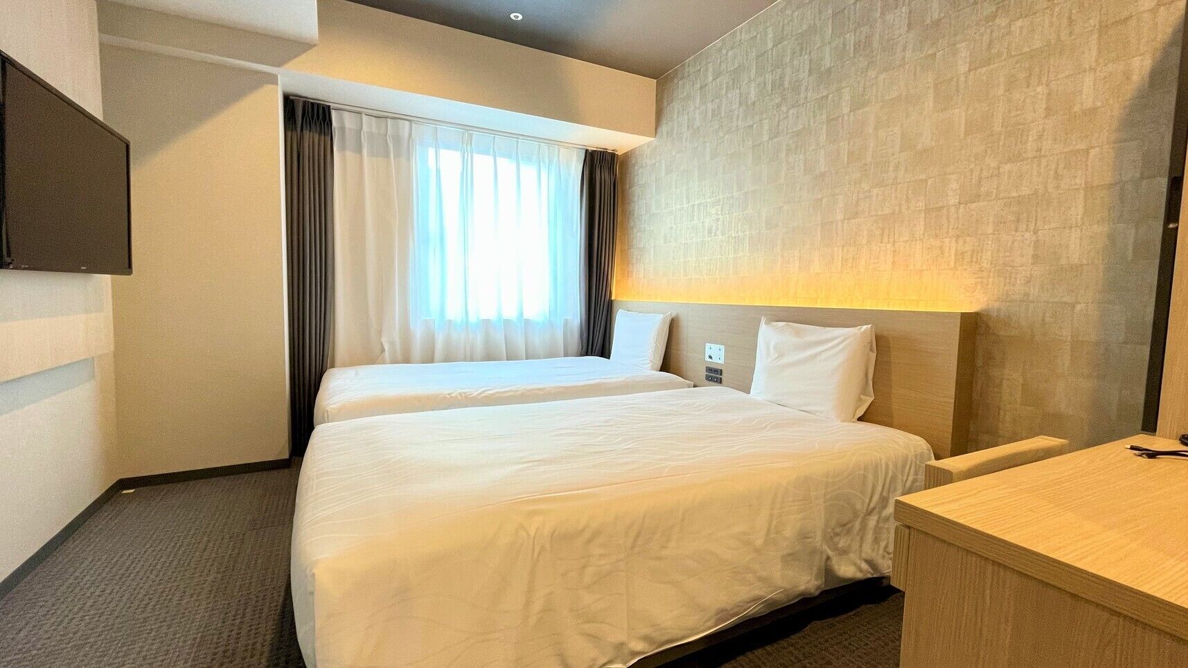 Quarto de hotel com duas camas, uma televisão de tela plana, uma escrivaninha e uma janela com cortinas.
