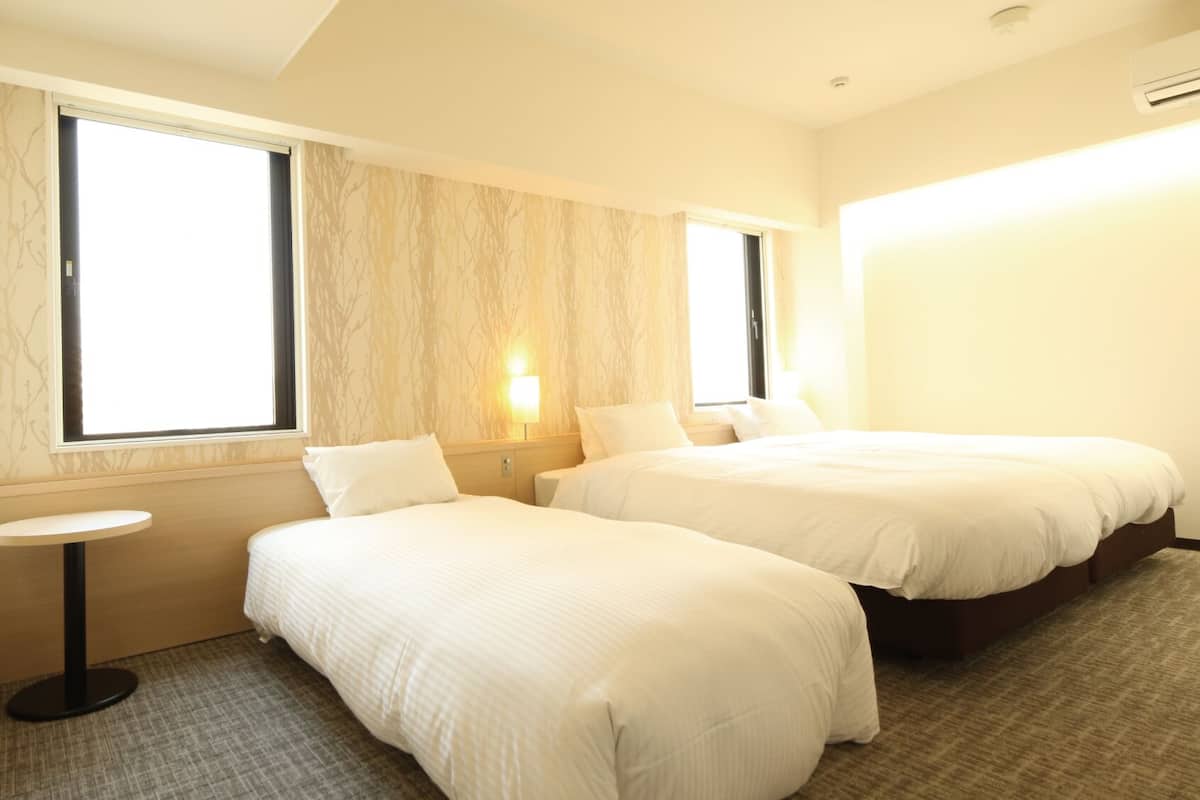 Quarto de hotel com duas camas, uma mesinha e uma janela.