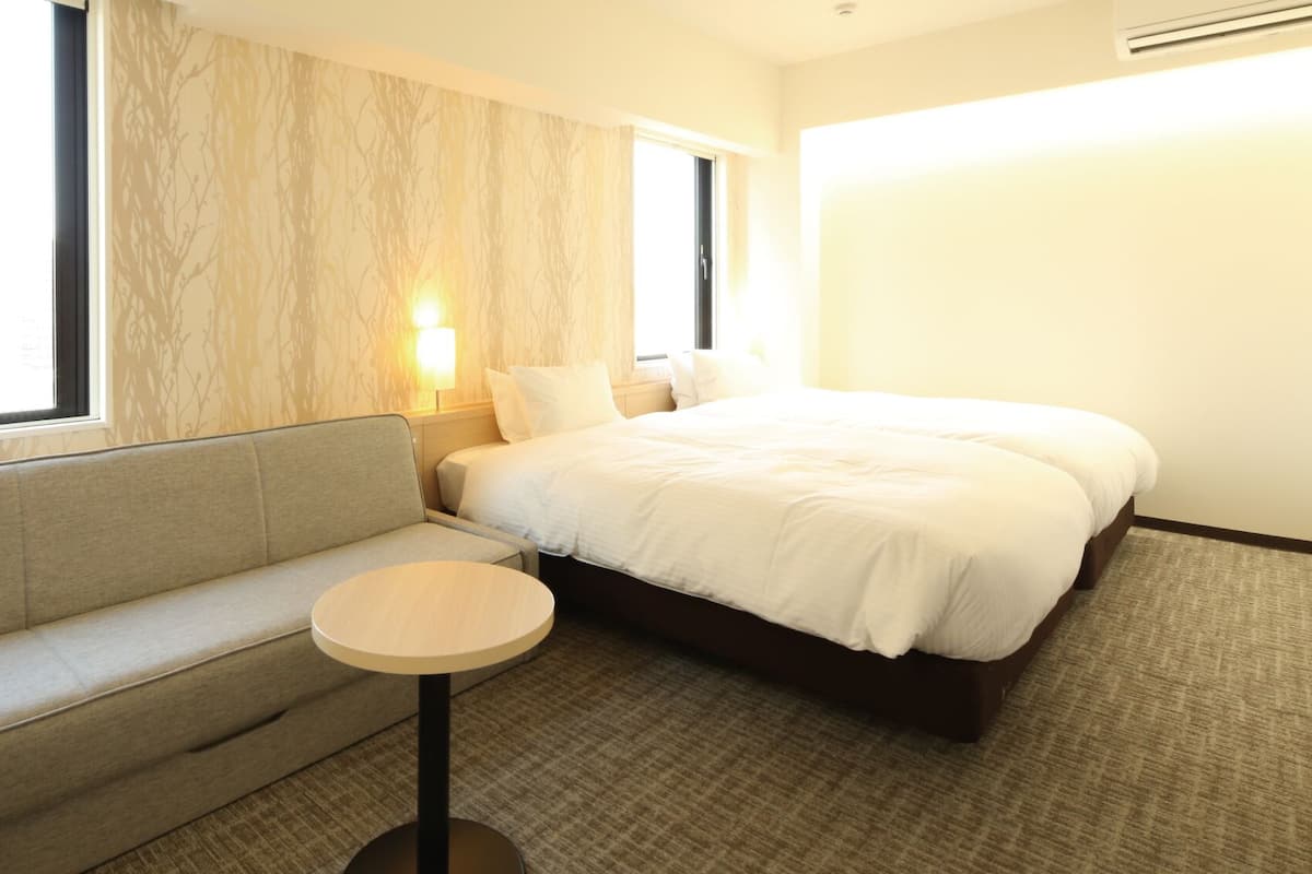 Quarto de hotel com uma cama, um sofá, uma mesinha e uma janela.