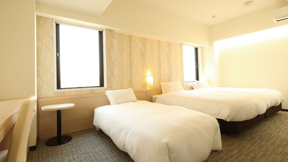 Quarto de hotel com duas camas, uma mesa redonda pequena e uma janela.