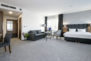 Quarto de hotel com cama, sofá, cadeira, mesa pequena e luminária.