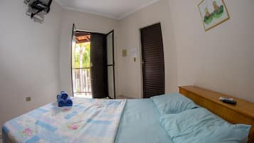 Quarto com cama, mesa de cabeceira de madeira, televisão fixada na parede e porta que dá para área externa.