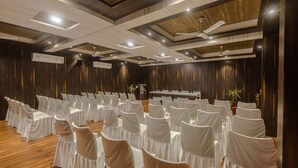 Uma sala de conferências com fileiras de cadeiras e mesas cobertas de branco, piso de madeira e teto com iluminação embutida e ventilação.