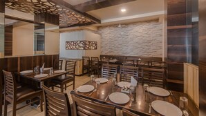 Restaurante com mesas e cadeiras de madeira, parede de pedra e ventoinha no teto.