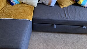 Um sofá modular com manta amarela mostarda e diversos almofados estampados.