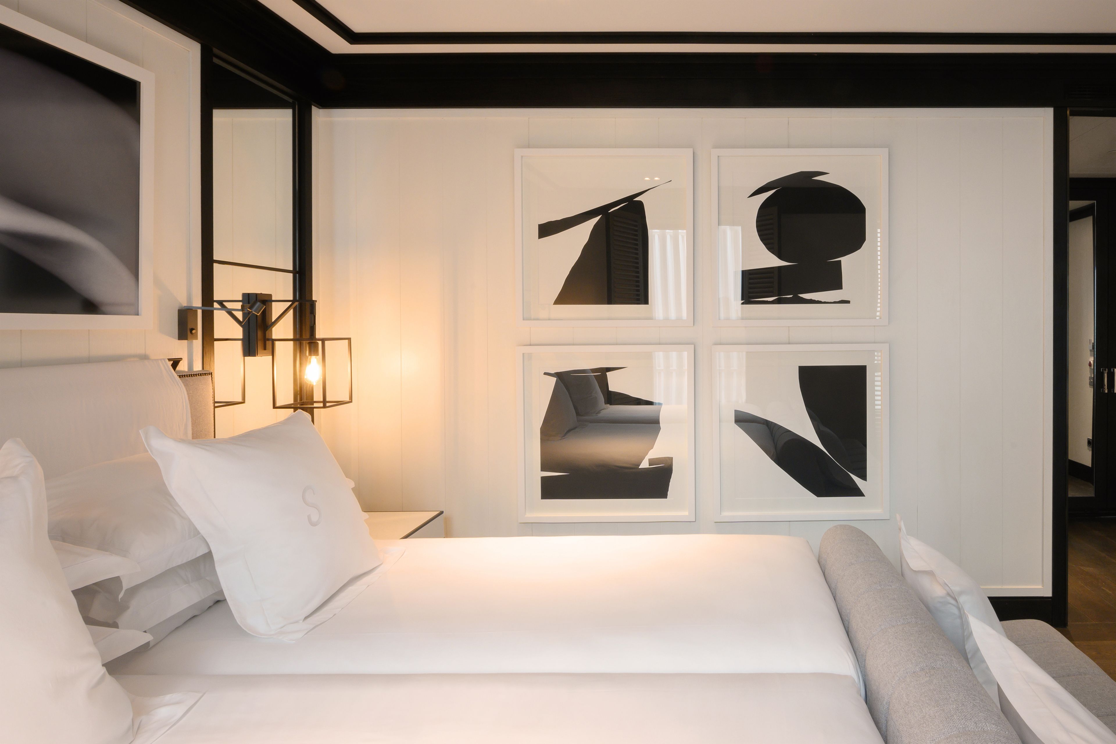 Quarto de hotel moderno com cama bem arrumada, exposição de arte na parede e design minimalista.