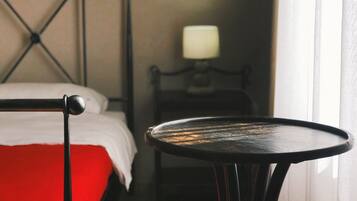 Quarto de hotel com cama, uma mesinha e uma mesa de cabeceira com abajur.