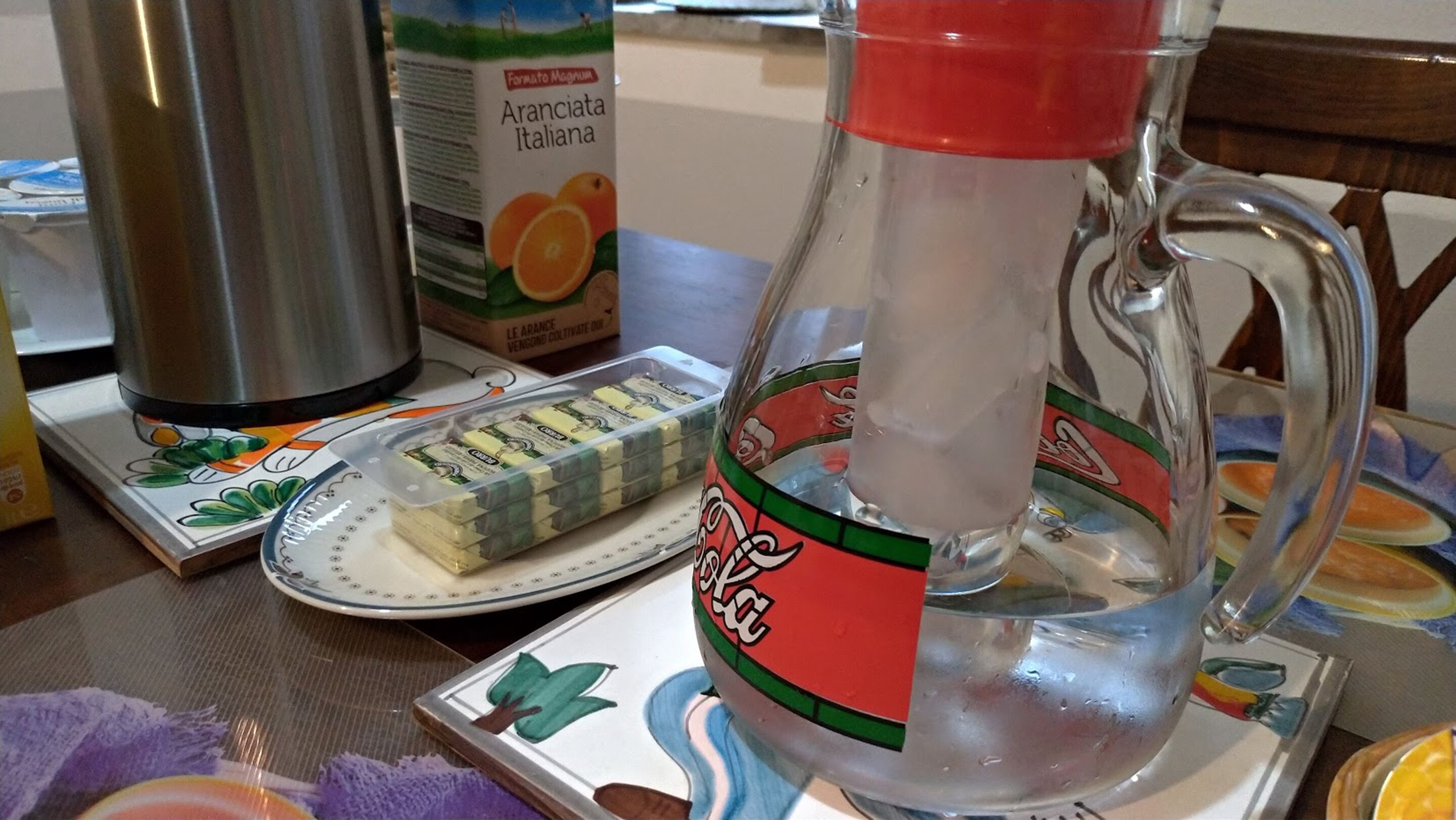 Uma bancada de cozinha com uma cafeteira, uma garrafa de água, um prato de queijo e uma caixa de suco de laranja.