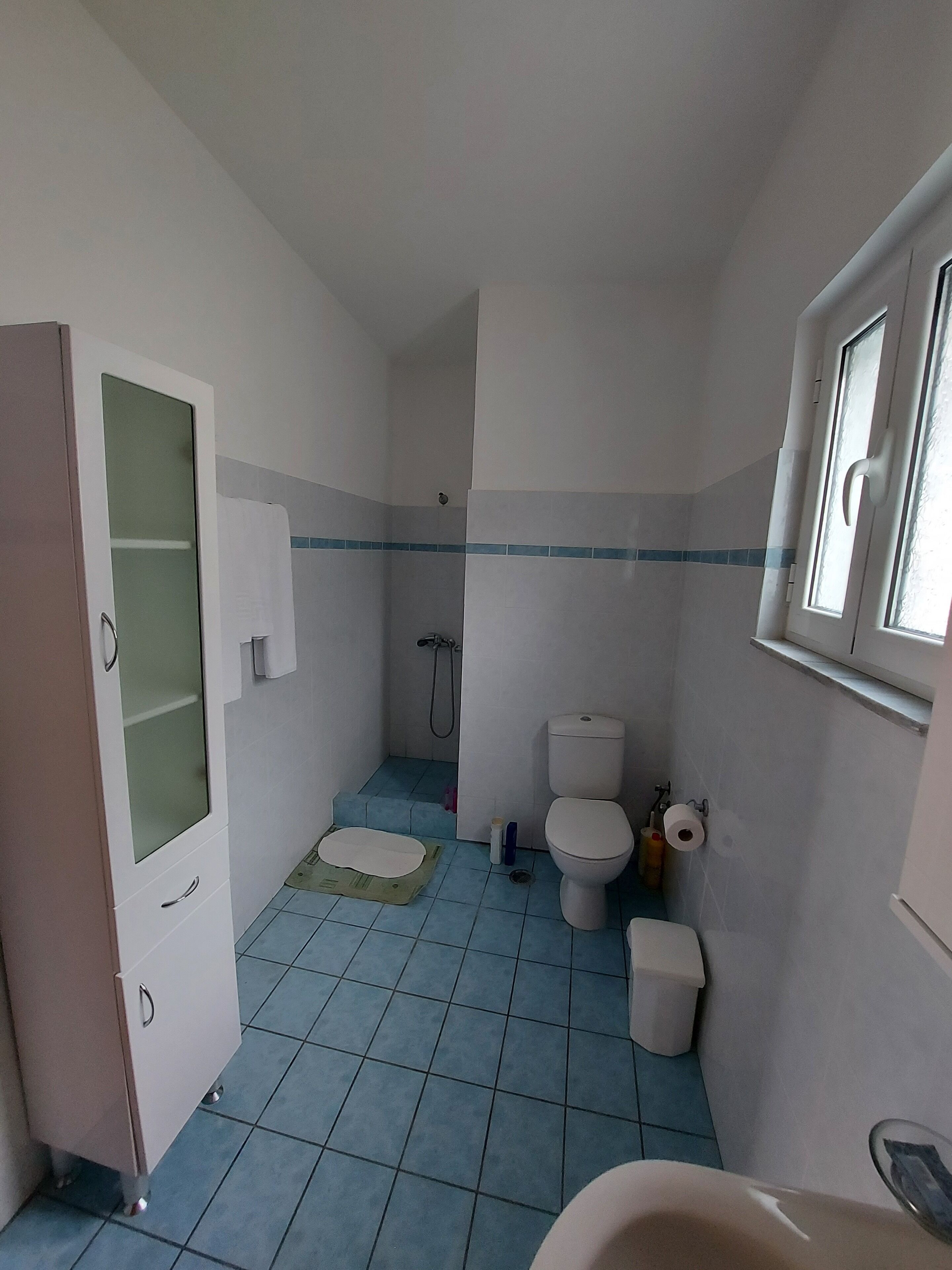 Uma casa de banho pequena com sanita, bidé e cabine de duche. Há um armário com espelho e um porta-toalhas.