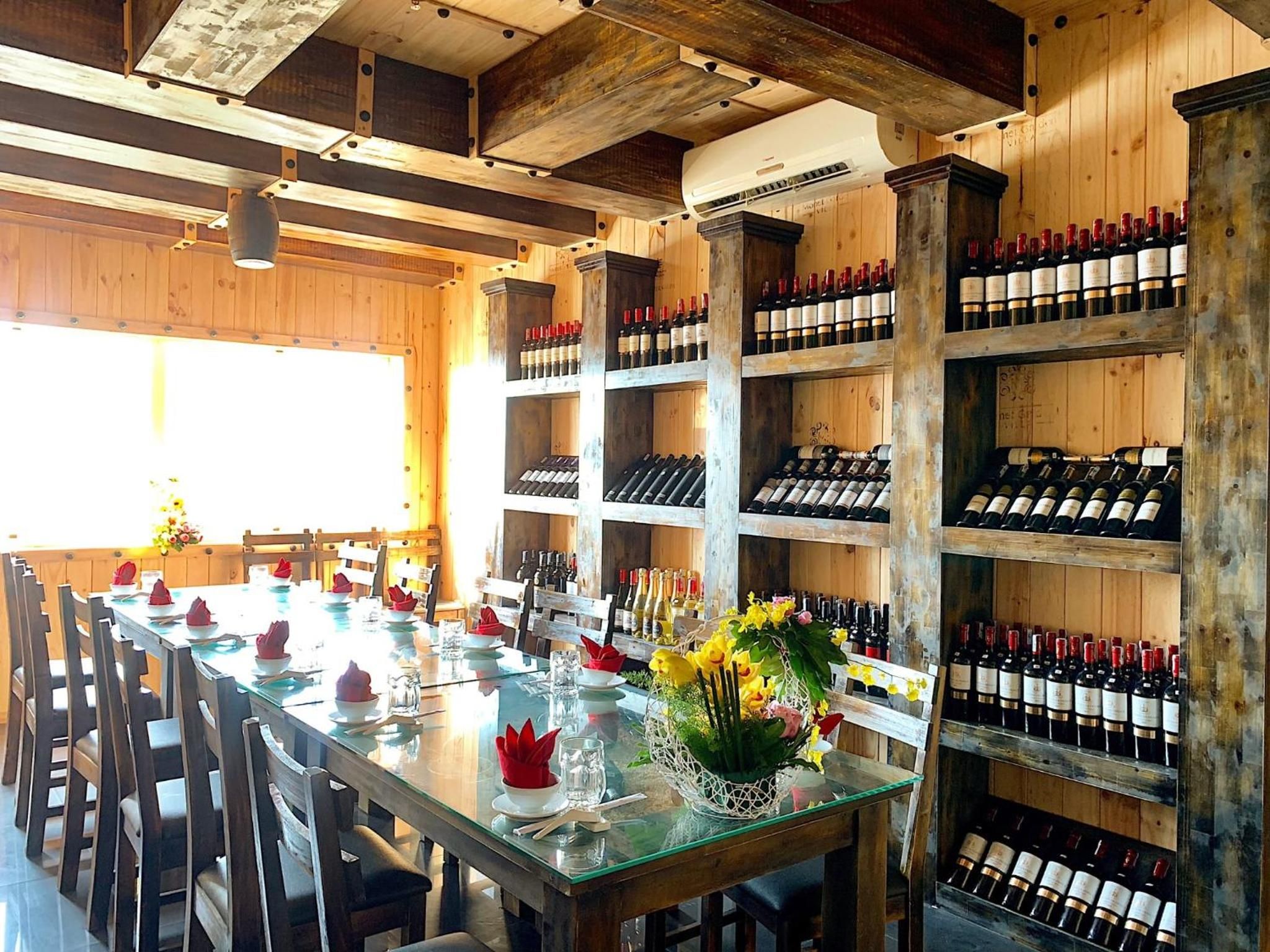 Restaurante com uma longa mesa de madeira posta para refeição, rodeado por estantes altas de madeira repletas de garrafas de vinho.