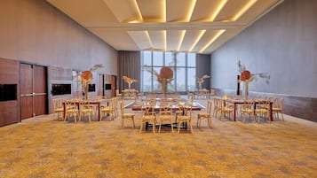 Uma sala de conferências ampla, com várias mesas e cadeiras, janelas grandes e um design moderno no teto.