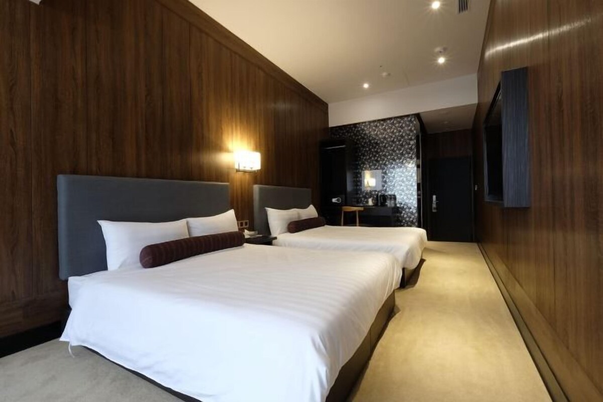 Quarto de hotel com duas camas, parede de madeira, uma pequena escrivaninha e um espelho.