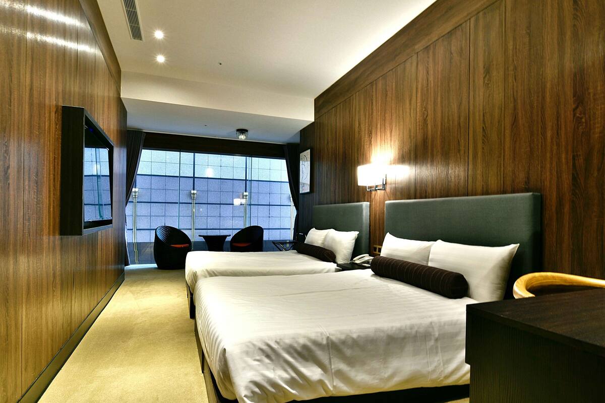 Quarto de hotel com duas camas, uma janela grande e vista para a paisagem urbana.