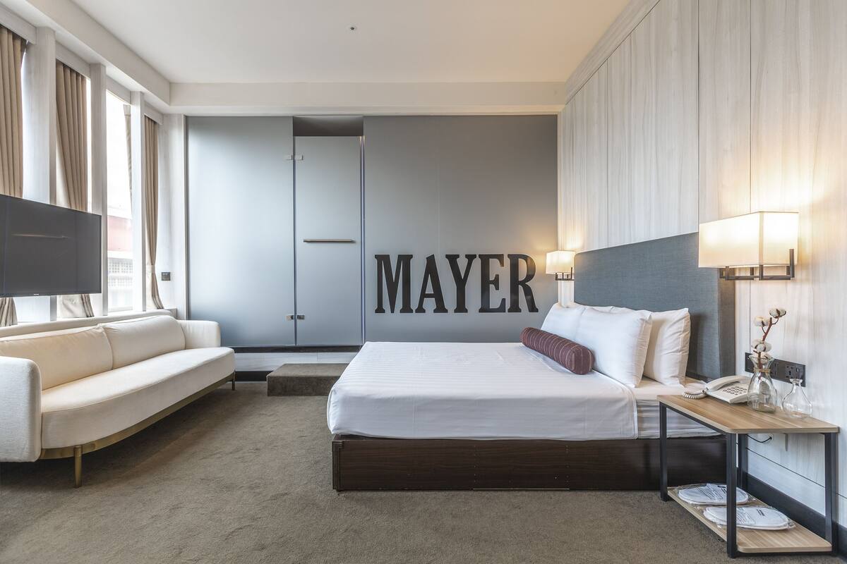 Quarto de hotel com cama, sofá, televisão e uma parede com a palavra "MAYER".