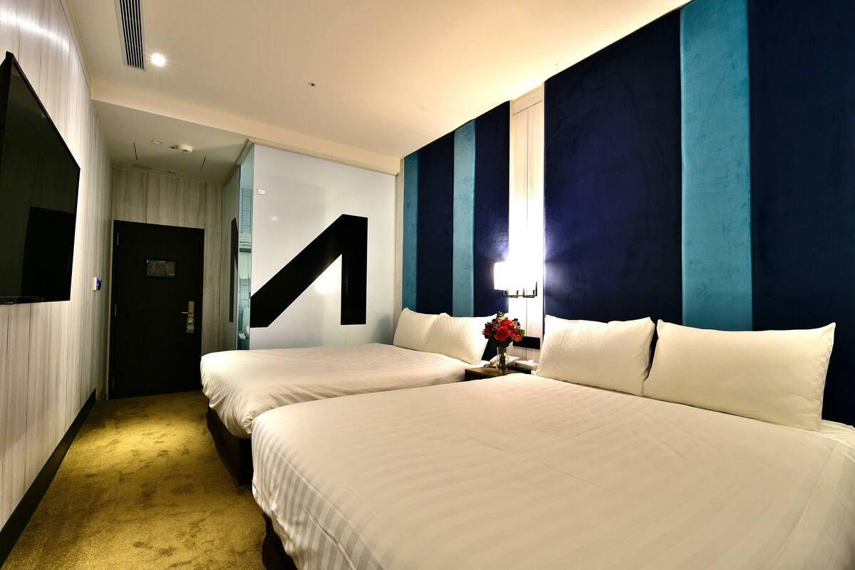 Quarto de hotel com duas camas, piso coberto por carpete, uma escada e parede com padrão geométrico.