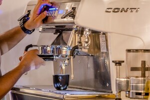 Alguém a preparar café numa máquina, com uma chávena colocada sob o bico.