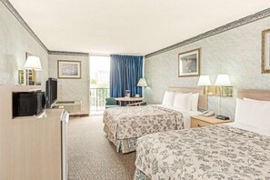 Quarto de hotel com duas camas, uma escrivaninha, televisão e varanda com cortinas azuis.