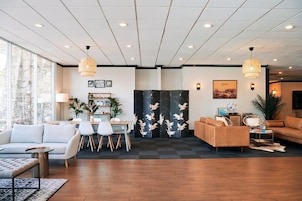 Um lobby moderno de hotel com área de estar, mesa de jantar e um painel decorativo.