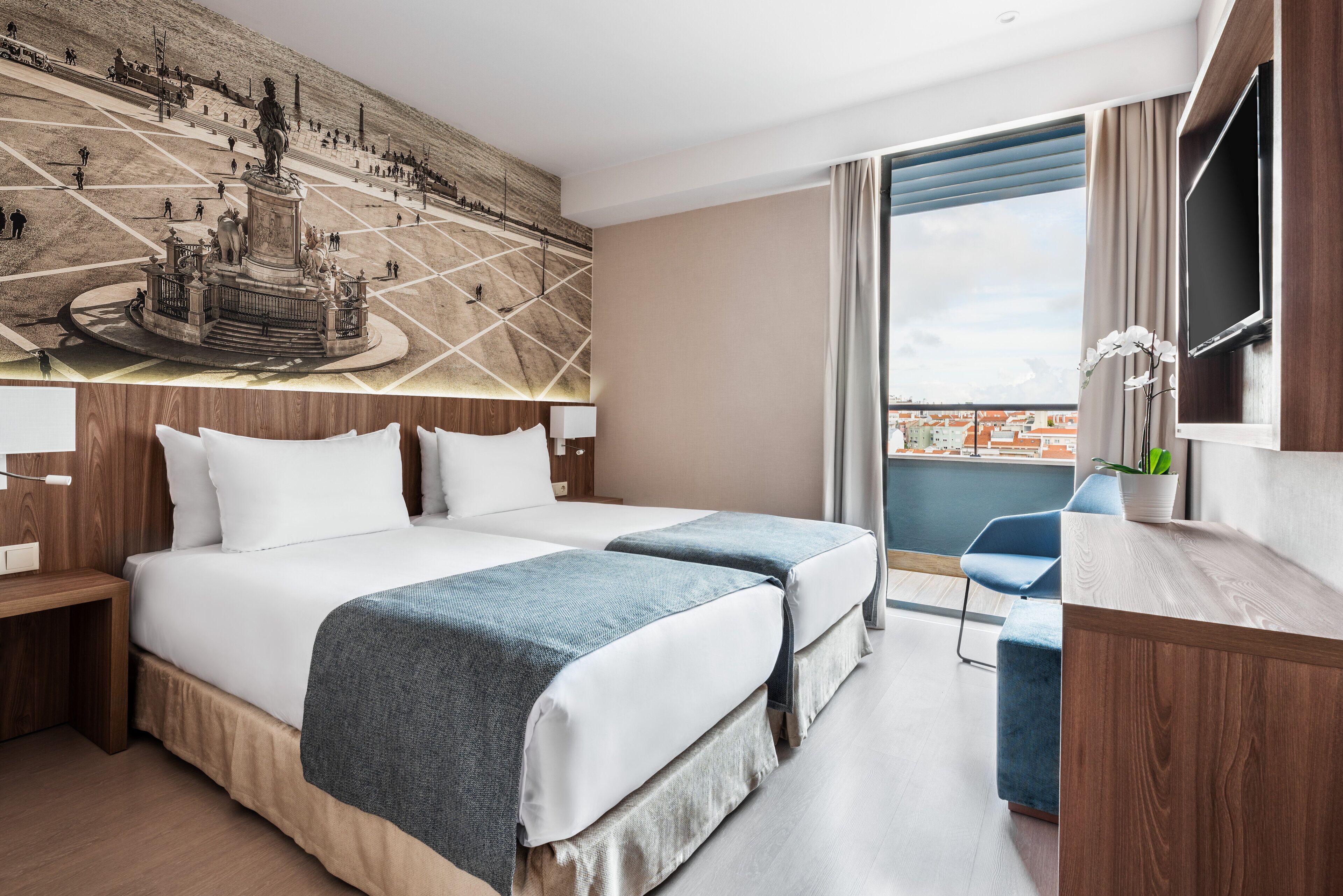 Quarto de hotel com uma cama grande, uma escrivaninha, uma cadeira e um mural com vista para a cidade.