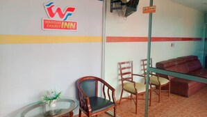 Uma área de recepção com o logotipo do 'Warisan Family Inn', um painel de vidro, um sofá e uma pequena mesa com uma planta.