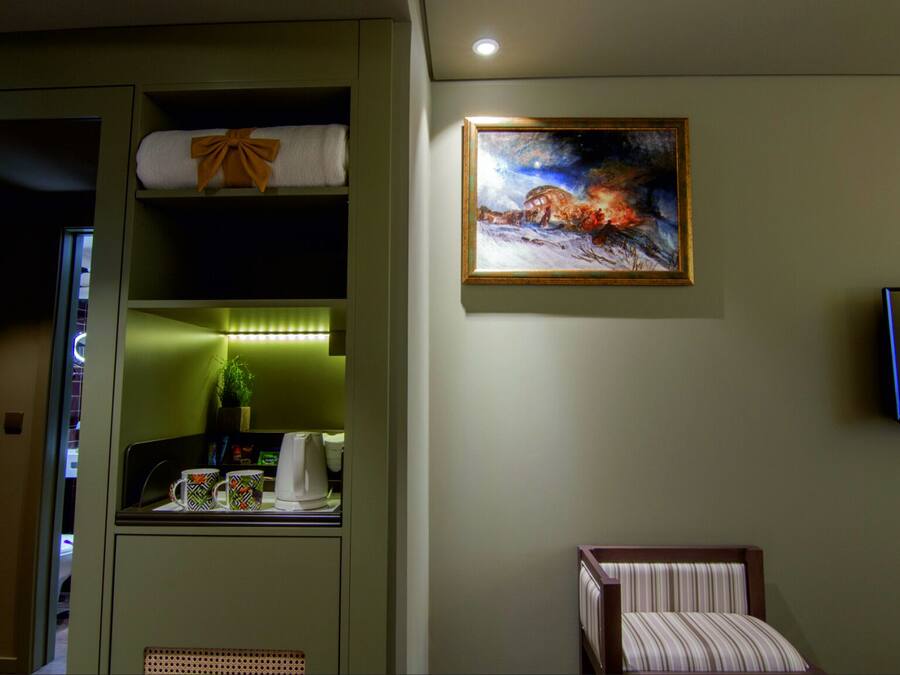 Quarto de hotel com cama, televisão, um quadro e uma estante com toalhas e uma cafeteira.