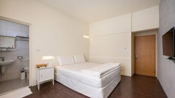 Quarto com cama, mesa de cabeceira, espelho, porta de madeira e uma pequena janela.