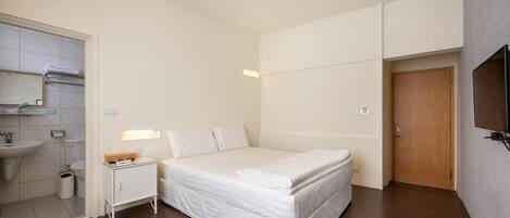 Quarto com cama, mesa de cabeceira, espelho, porta de madeira e uma pequena janela.