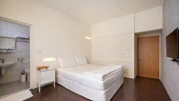 Quarto com cama, mesa de cabeceira, espelho, porta de madeira e uma pequena janela.