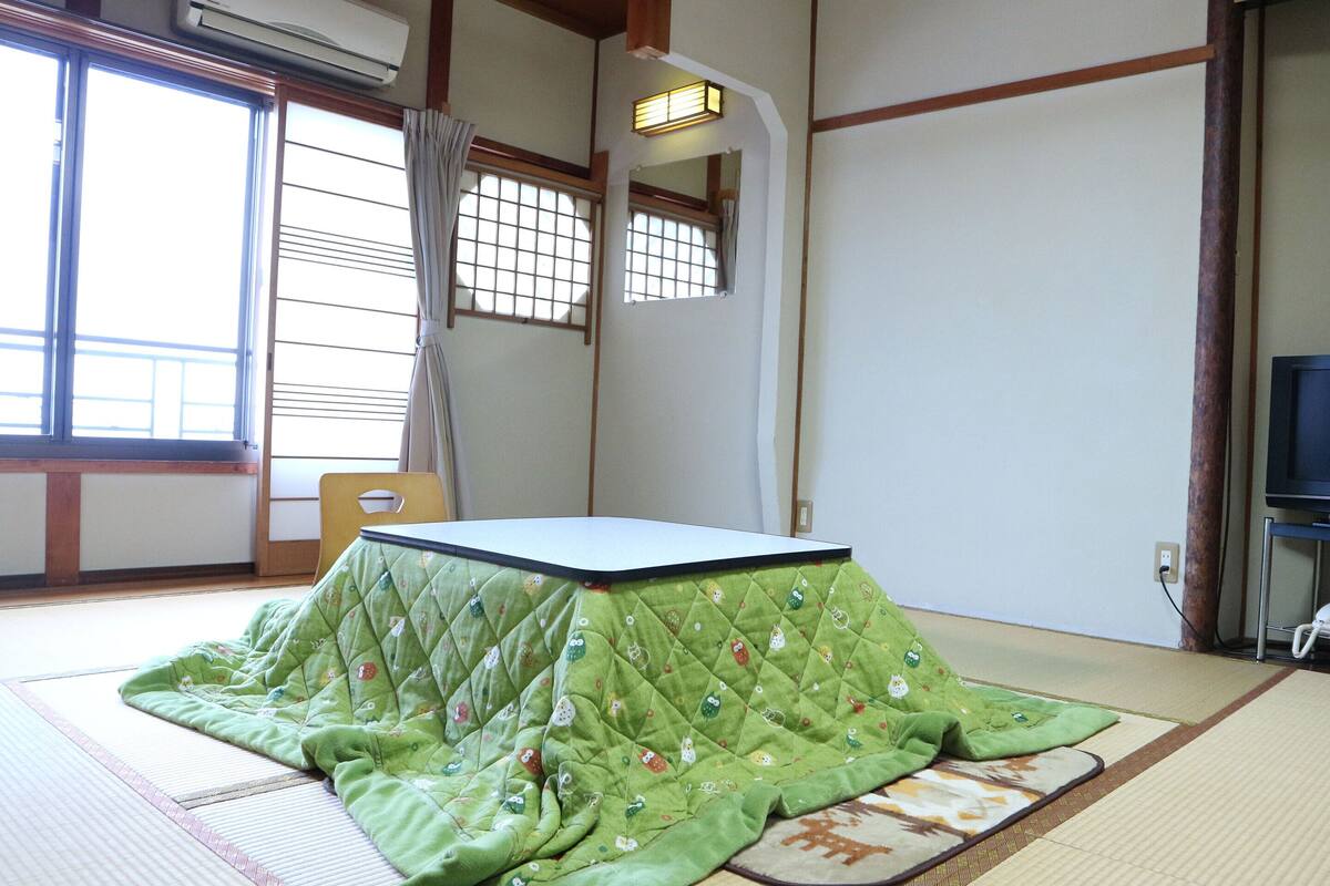 Um espaço com tatames, uma mesa baixa e um cobertor acolchoado verde.
