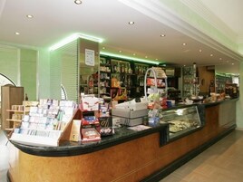 Uma área de recepção de hotel com um balcão exibindo diversos itens, uma vitrine de vidro e prateleiras com produtos.