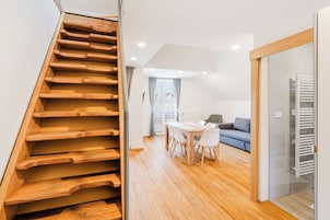 Um interior moderno com escada de madeira, área de jantar com mesa e cadeiras, um sofá e uma divisória de vidro.