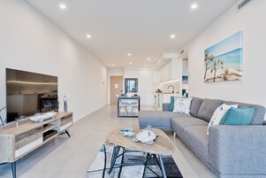 Uma sala de estar moderna com um sofá cinza, mesa de centro de madeira e uma TV de tela plana.