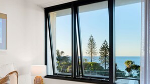 Quarto de hotel com uma janela grande que oferece vista para o mar e árvores.