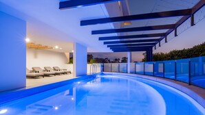 Piscina interior moderna com design curvo, espreguiçadeiras e barreira de vidro.