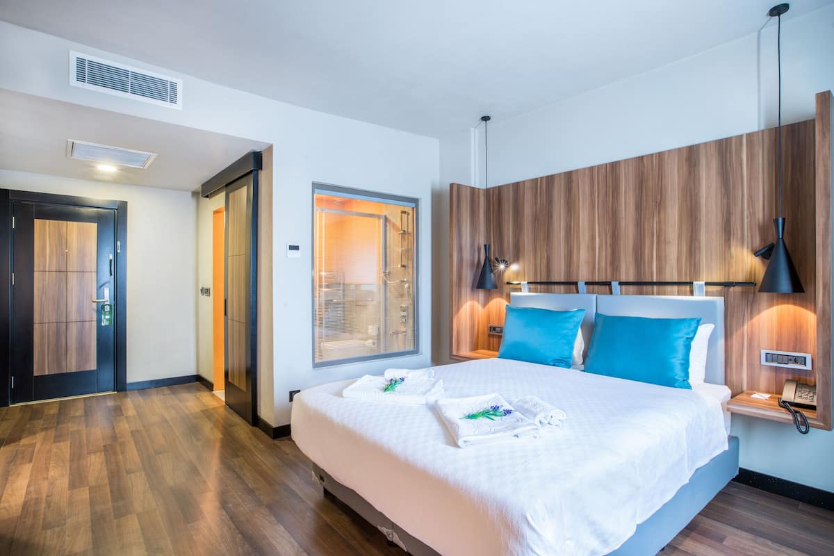 Quarto de hotel moderno com uma cama grande, painel de parede de madeira e um guarda-roupa embutido.