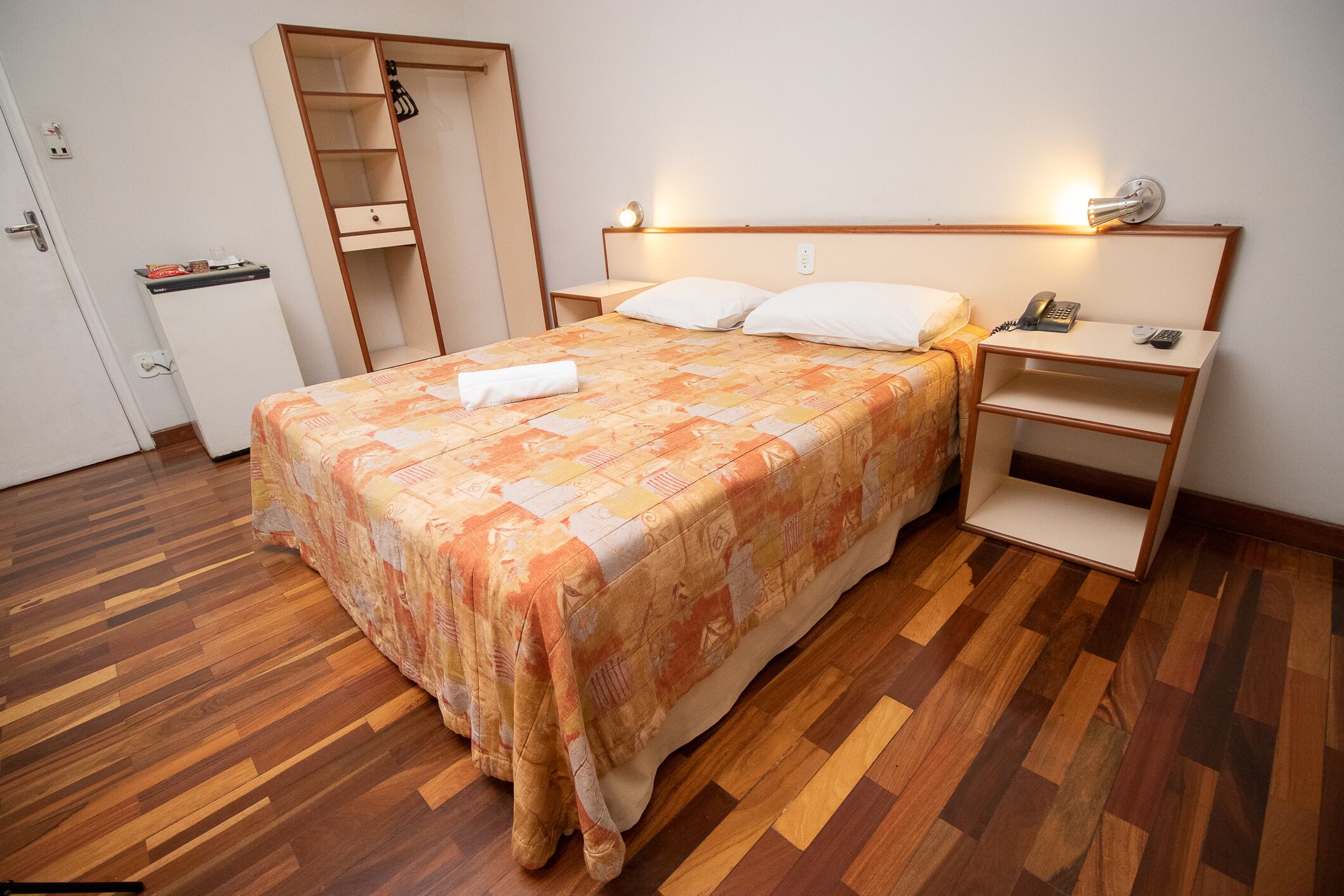 Quarto bem arrumado com cama, mesas de cabeceira e guarda-roupa.