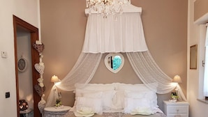 Quarto com cama de dossel, mesas de cabeceira, relógio e objetos decorativos.