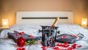 Uma cama com uma garrafa de champanhe, copos e pétalas de rosa.