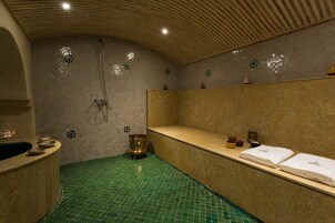 Casa de banho com chão em mosaico verde, banheira, espaço de duche e prateleira com toalhas e produtos de higiene.