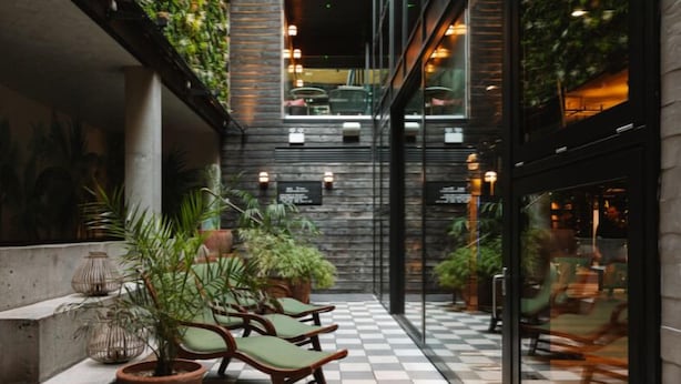 Uma área de estar ao ar livre moderna, com piso xadrez, plantas em vasos e espreguiçadeiras de madeira.