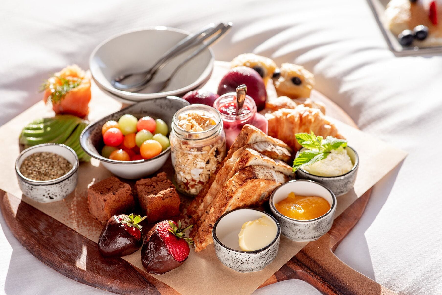 Uma bandeja de café da manhã com torradas, geleia, iogurte e diversas frutas.