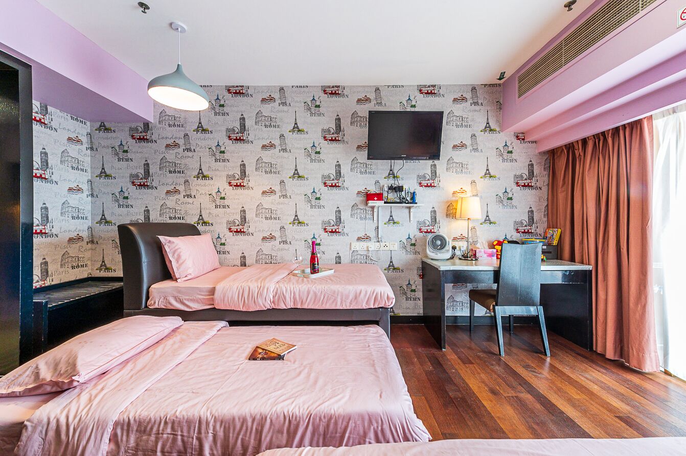 Quarto de hotel com duas camas, uma escrivaninha, uma cadeira, uma televisão e parede com papel de parede da paisagem urbana.
