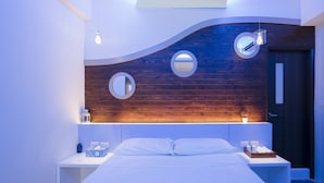 Quarto moderno com cabeceira de madeira curva, duas mesinhas de cabeceira, cama com roupa de cama branca e um criado-mudo com abajur.