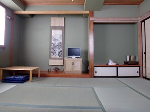 Um quarto japonês tradicional com tatames, uma mesa de madeira baixa, uma televisão e um armário com espaço para guardar.