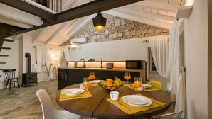 Uma sala de jantar com uma mesa redonda posta para quatro pessoas, uma parede de pedra e uma cozinha ao fundo.
