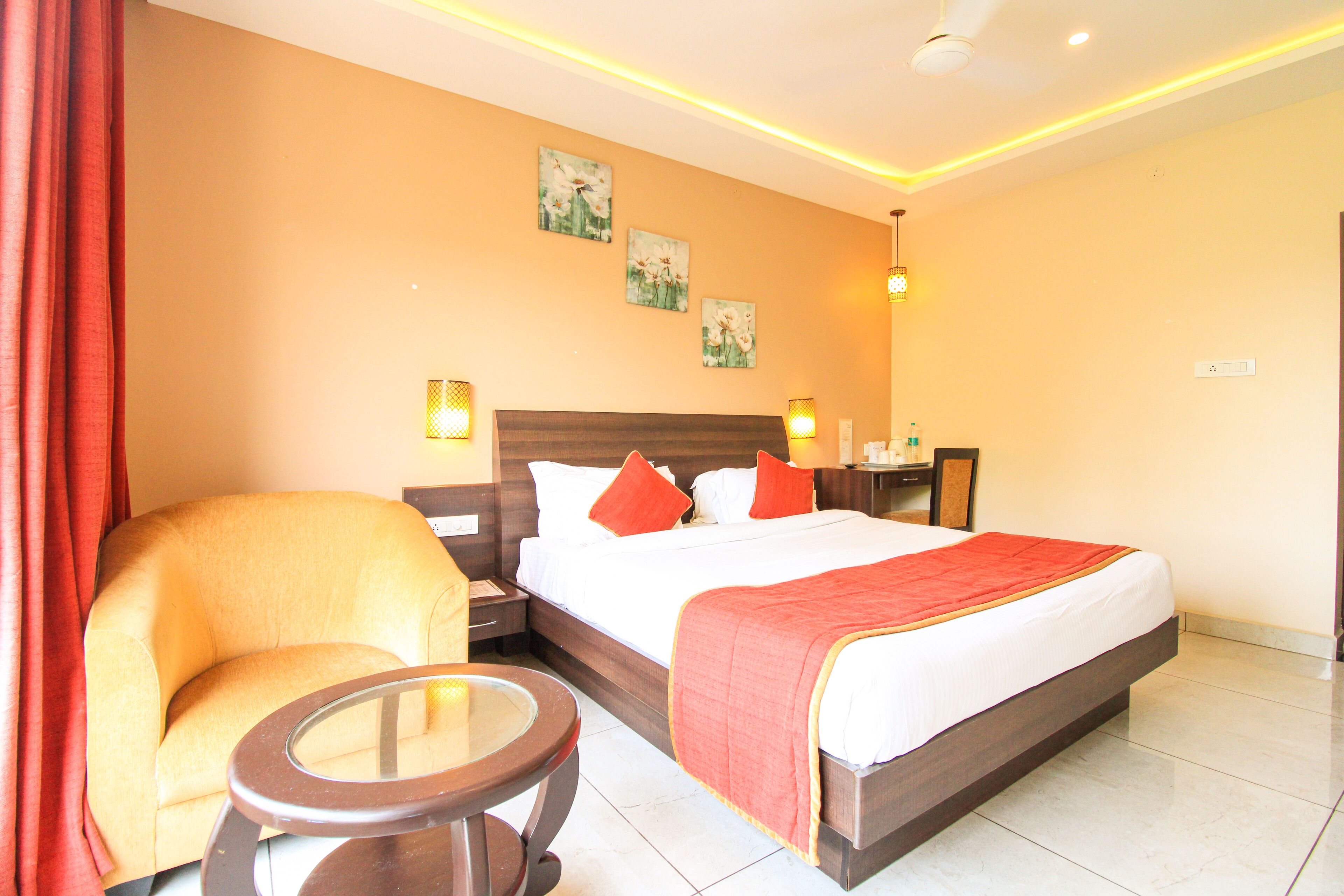 Quarto de hotel com cama, cadeira, mesa redonda e luminárias fixadas na parede.