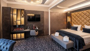 Quarto de hotel com uma cama grande, uma escrivaninha com televisão de tela plana, um espaço de estar com uma poltrona e um tapete estampado.