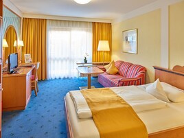 Quarto de hotel com cama, escrivaninha com computador, cadeira, sofá e pequena mesa com abajur.